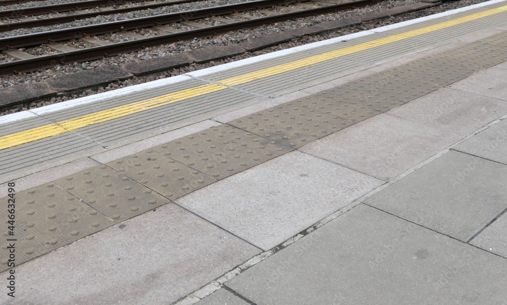 Train platform showing yellow safety line on paving and railway tracks ...