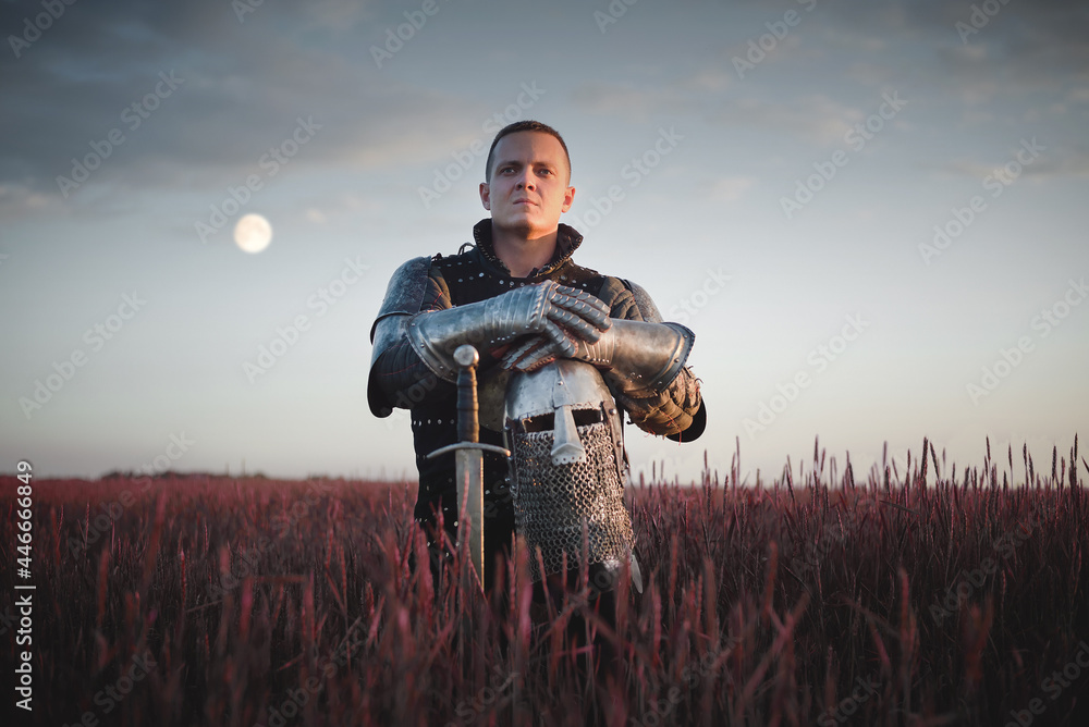 Medieval knight kneels in the field with his hand on the helmet on a ...