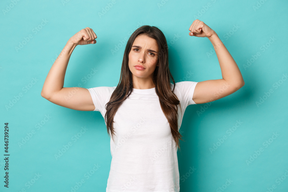 Image of young confident woman in white t-shirt, flexing biceps and ...