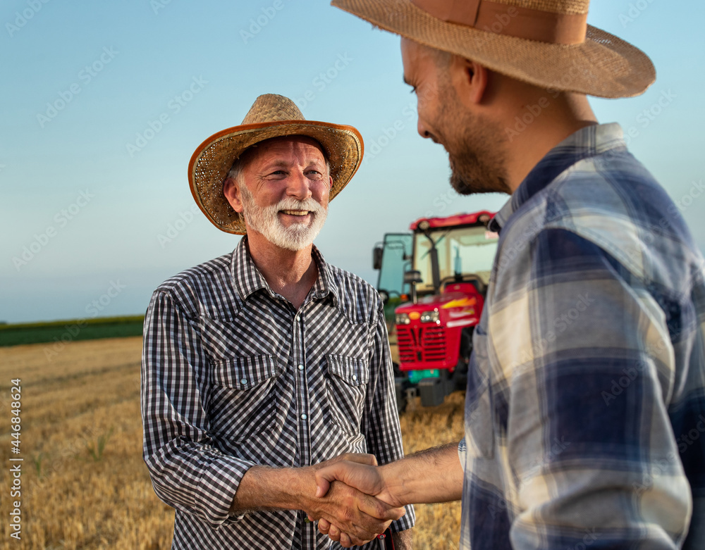 Male farmers standing in field in front of tractor shaking hands. Stock ...