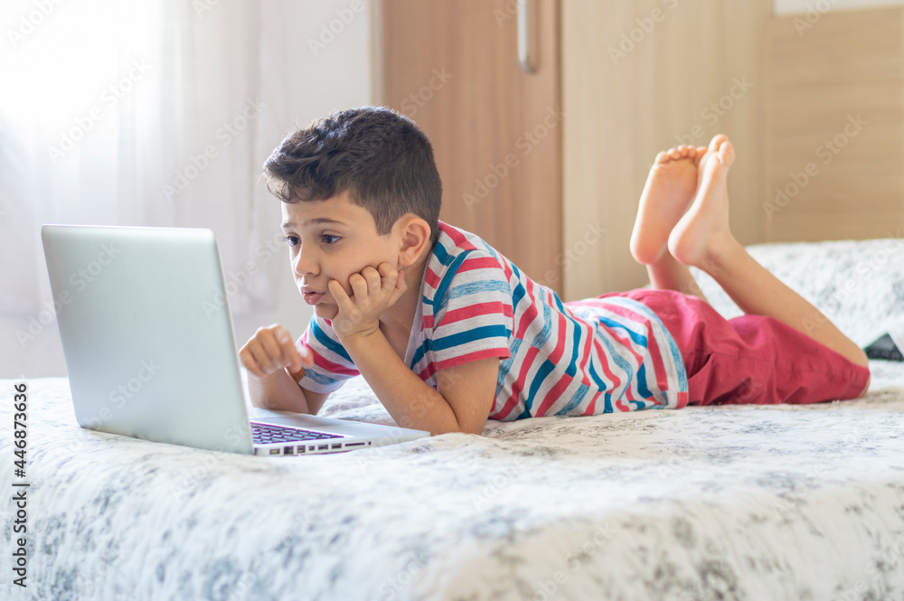 Young boy child lying on bed using a laptop. Online class lesson Stock ...