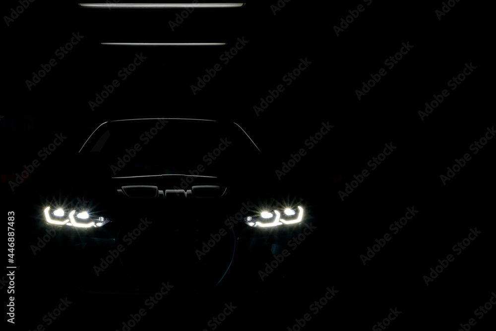 Unclear shape of front view sport car with headlights on dark ...