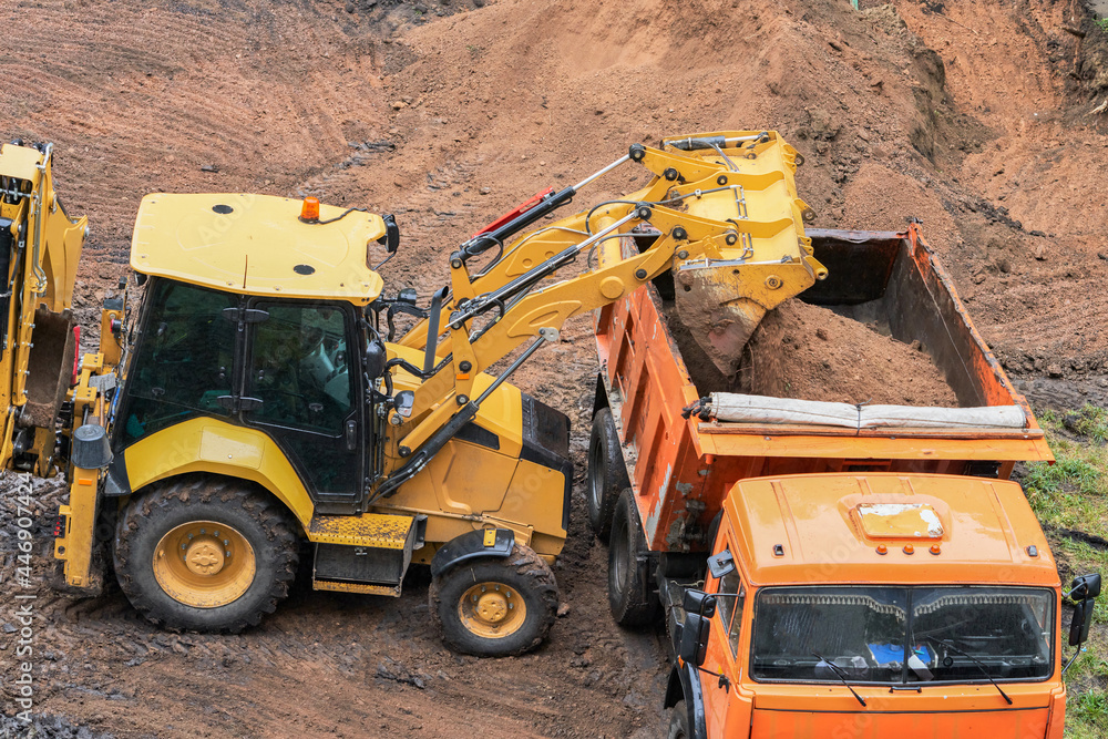 A miniature backhoe loader loads the soil into a dump truck. Stock ...