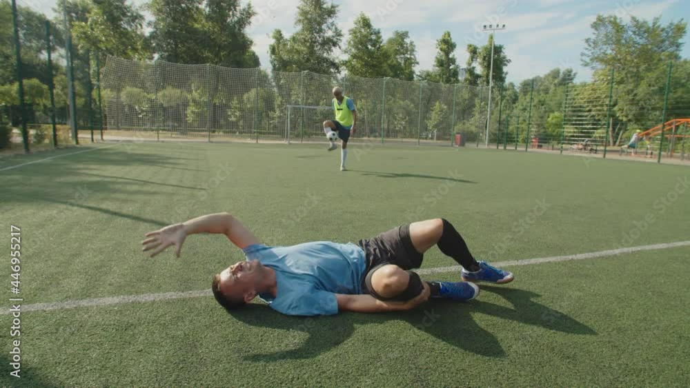 Injured soccer player in sportswear lying on football pitch after push ...