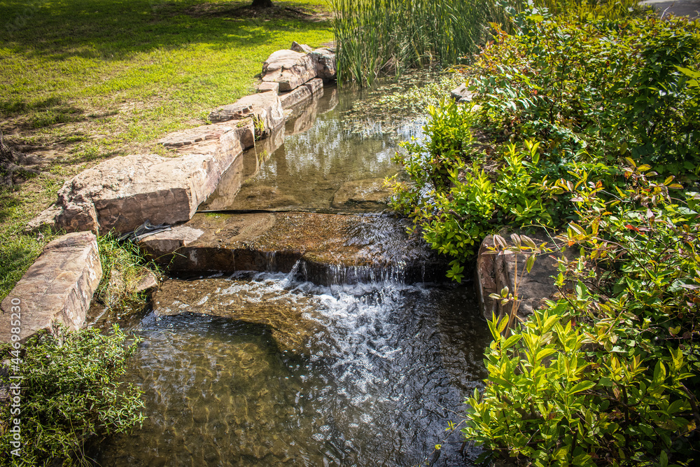 Manmade stream and waterfall flowing through park with lots of foliage ...