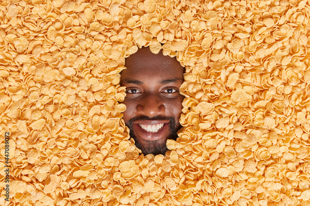 Positive dark skinned man with thick beard buried in dry cornflakes ...