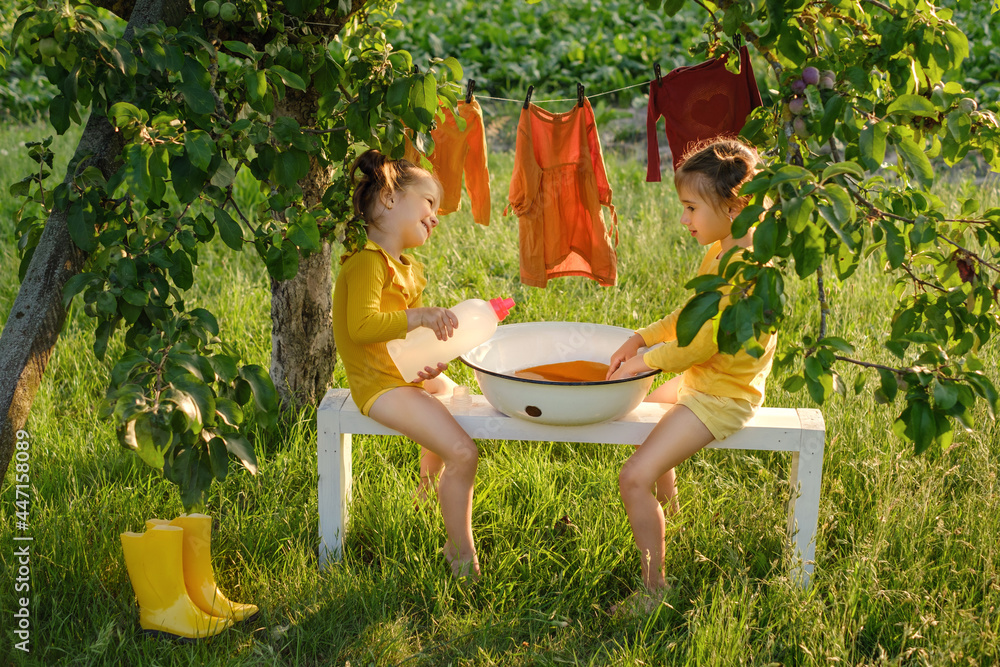Two little girls sisters wash clothes in a basin in the garden with ...
