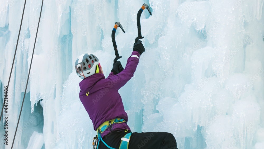 Female ice climber silhouette swinging ice axes on her way up vertical ...