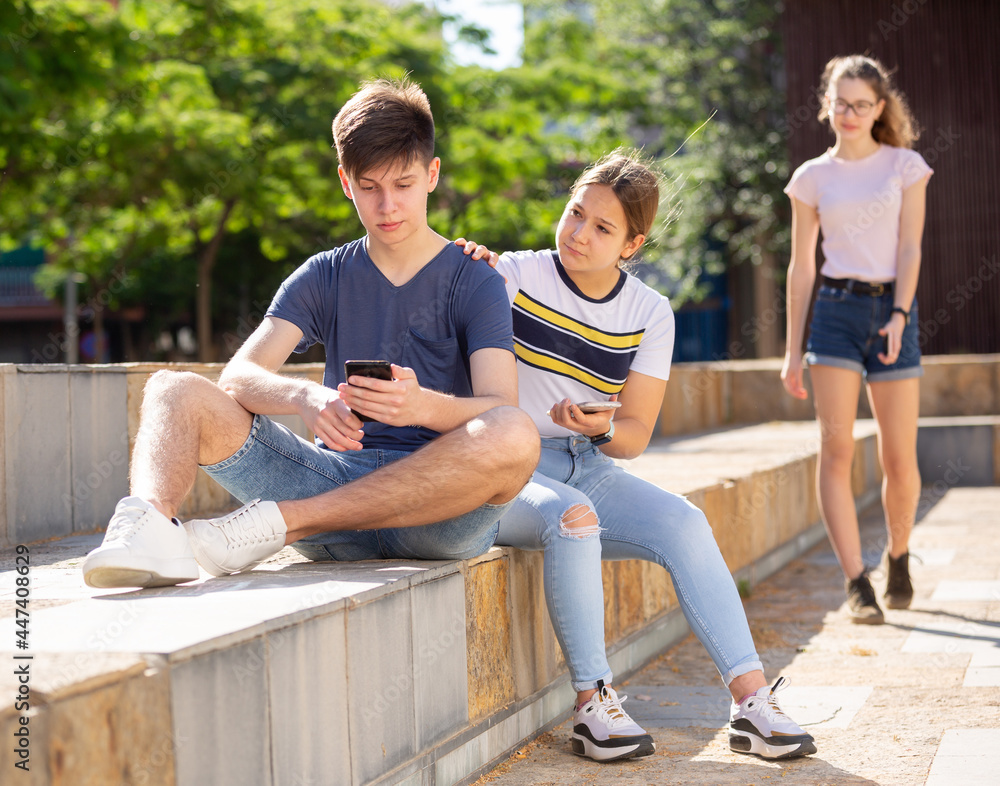 Interested teen boy sitting with phone on summer city street with ...