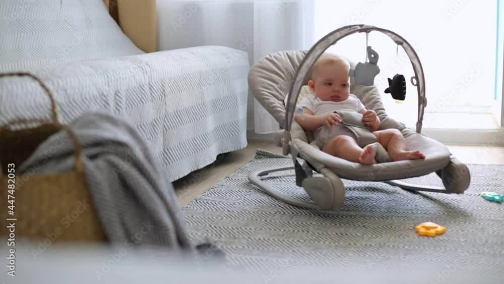 Cute baby sitting in rocking chair looking around and at hanging toys ...