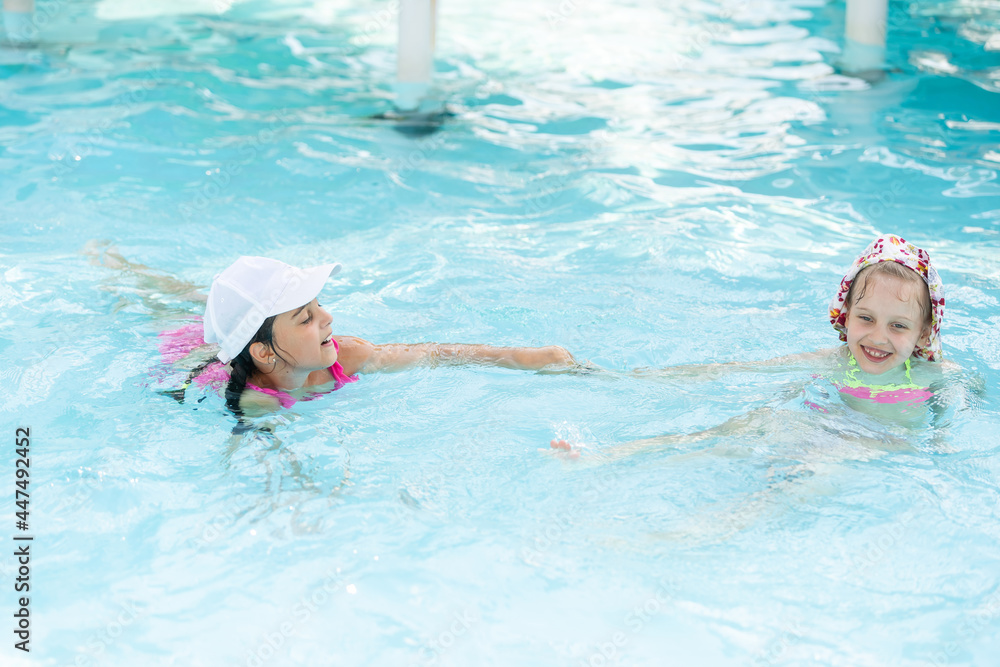 two girls splash in an outdoors swimming pool in summer. Happy children ...