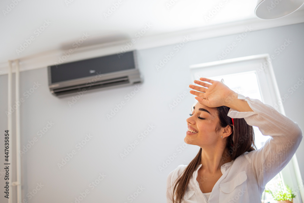 Portrait of young attractive woman adjusts air conditioner temperature ...