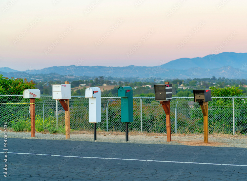 Row of mailboxes on the side of a street next to a fence during sunset ...