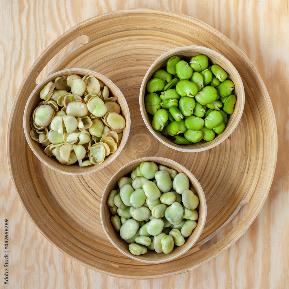 Raw fava beans in bowls. Peeled, unpeeled and separated seed skins of ...