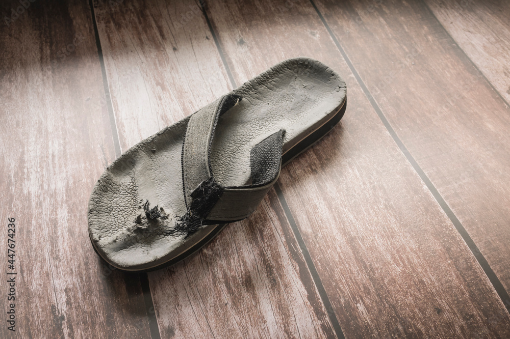 An old damaged flip flop on the floor. Toe post torn and ripped off by ...