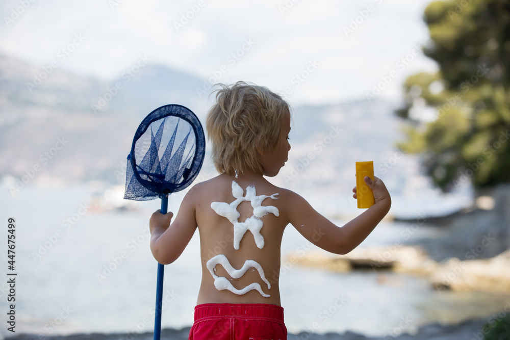 Little toddler child, holding sun cream, applying it on his body, sun ...