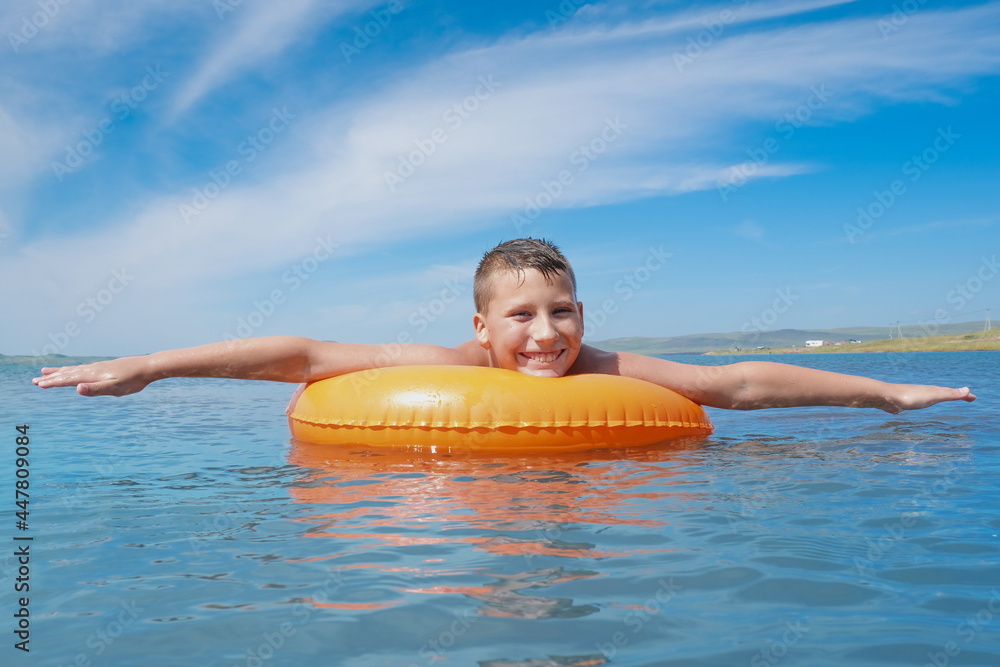 Boy swim in a blue lake at summer sunny day. He floats with orange ...