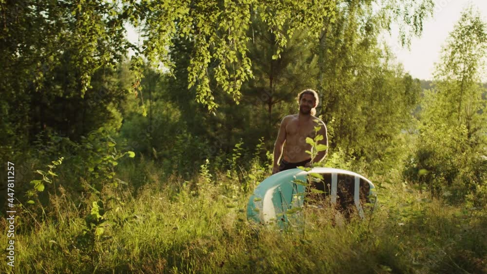 Brutal man holding surfing board, standing in forest. Muscular ...