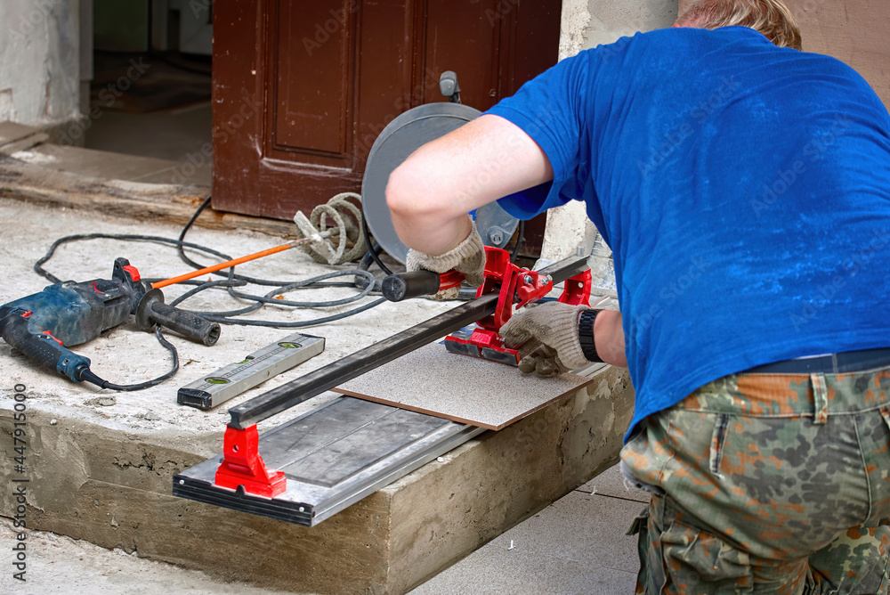 Worker laying new tiles on steps at entrance of building. Construction ...