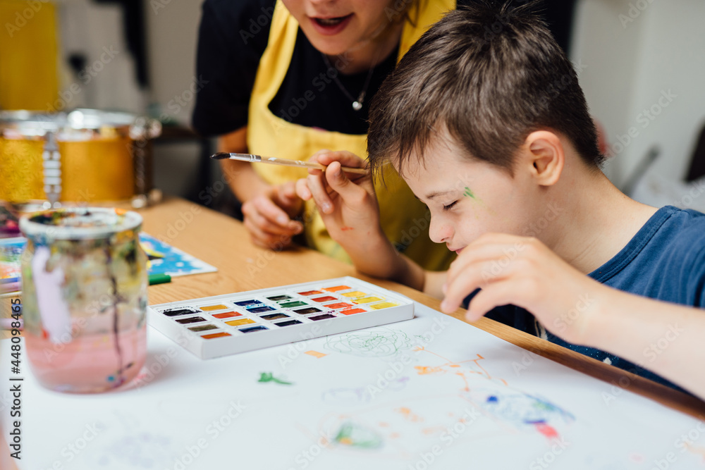 Foto de Young female teacher explain, talk at desk with a down syndrome ...