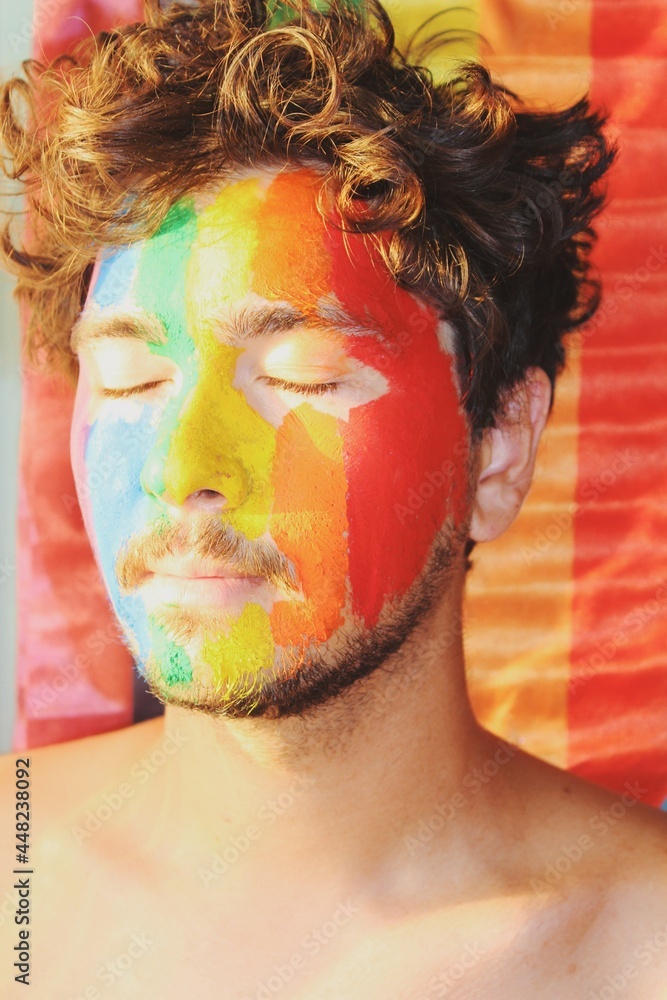 Closeup Portrait of young man face painted as lgbtq rainbow pride flag ...