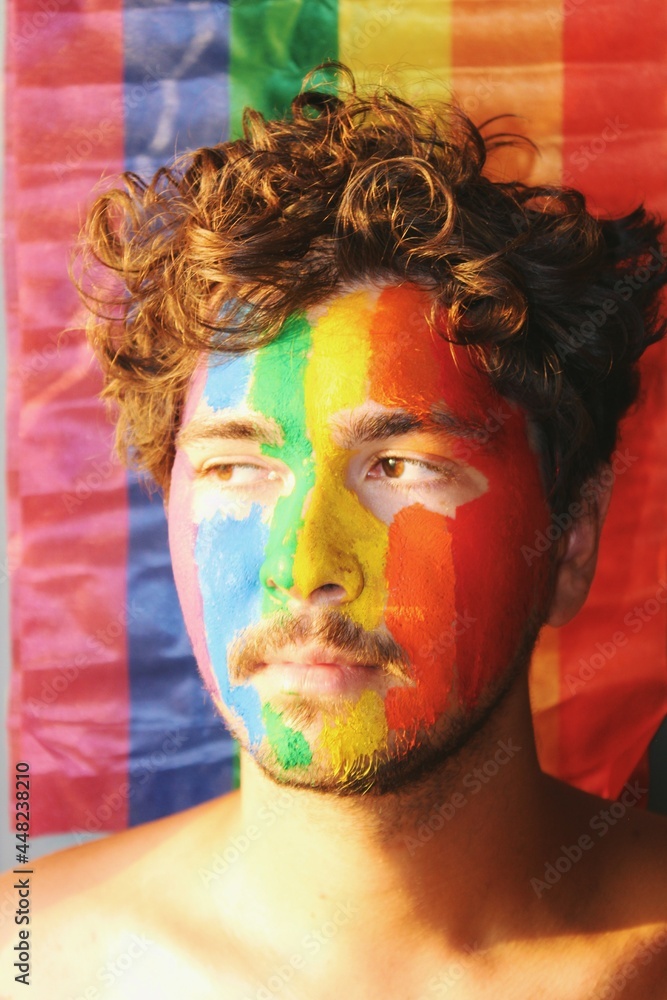 Closeup Portrait of young man face painted as lgbtq rainbow pride flag ...