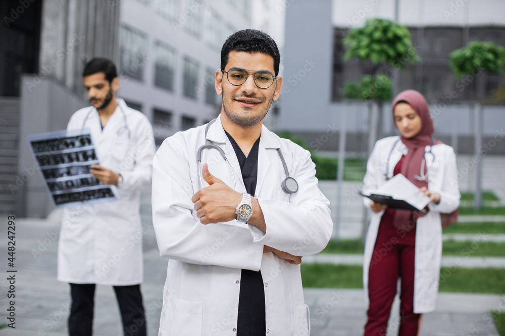 Fornt view of smiling young arabic male doctor, standing outdoors near ...