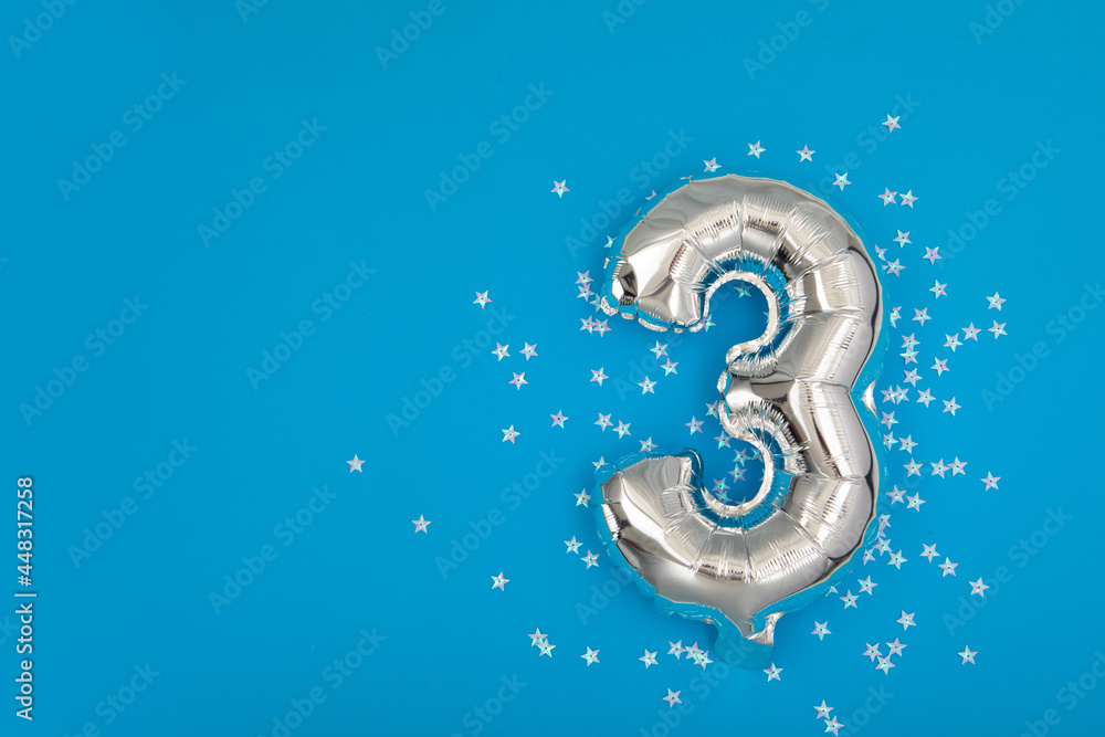 Silver balloon 3 on a blue background with confetti stars. Number three ...