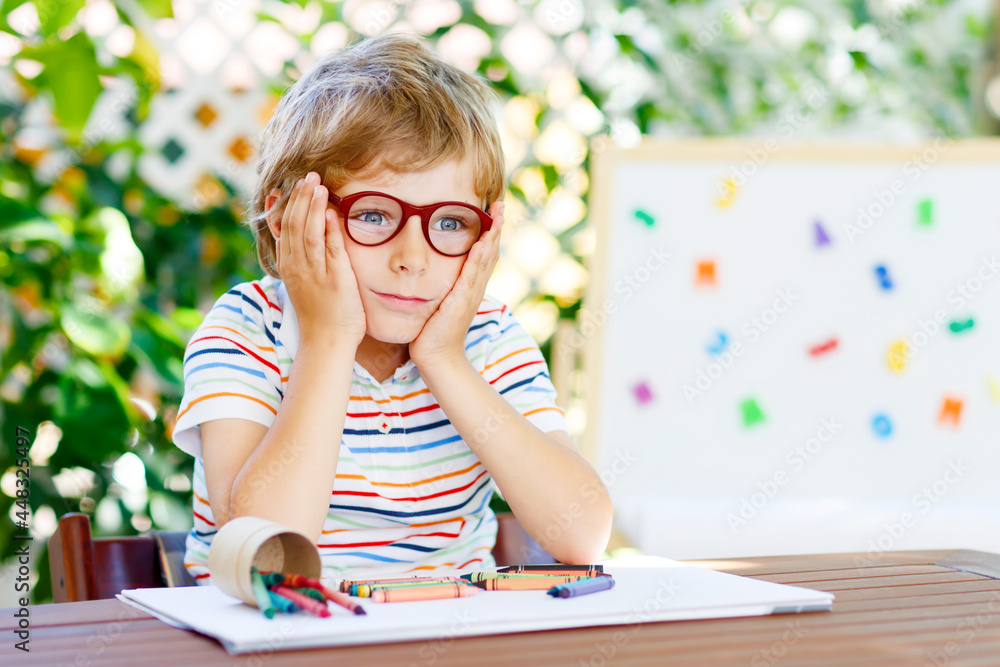Confused little kid boy with glasses with colorful wax crayon pencils ...