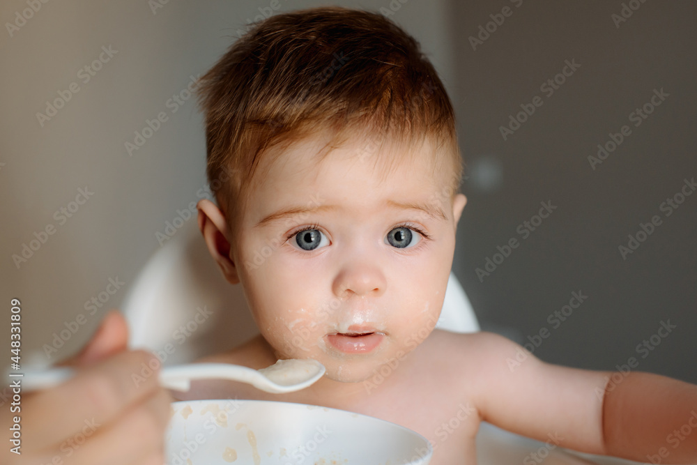 Caucasian baby boy with messy face eating porridge on a high chair ...
