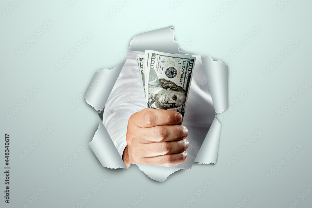 Hand holds a stack of money, breaking through the paper background. The ...