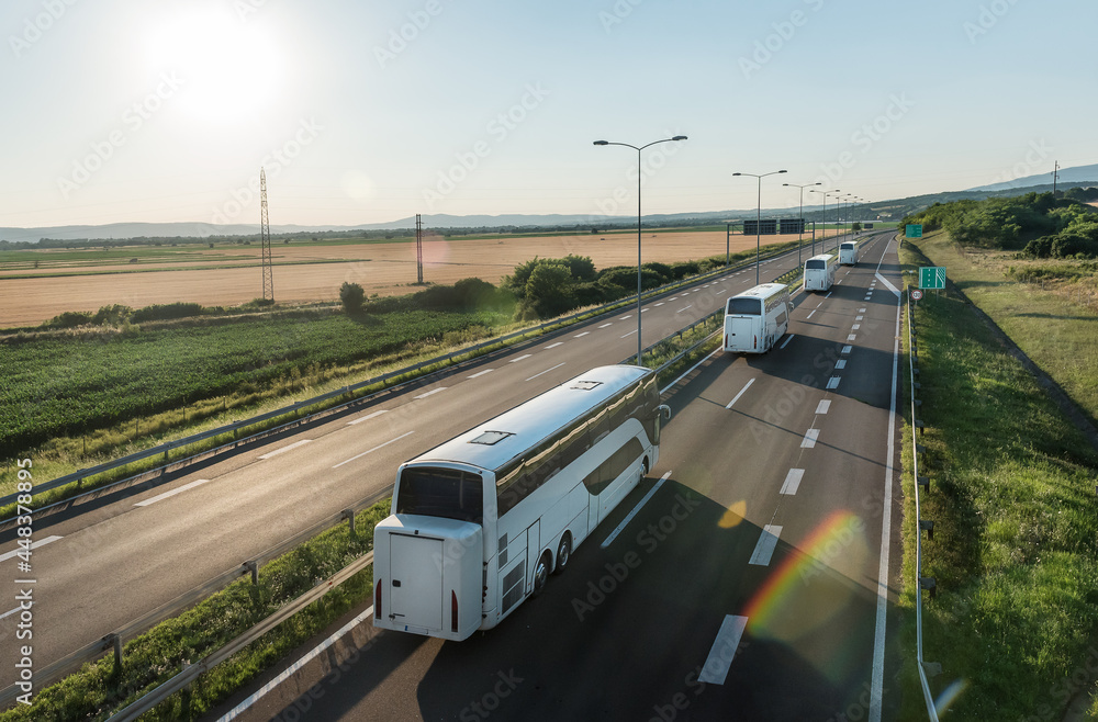 Series of modern White buses departing on a wide highway in a rural ...