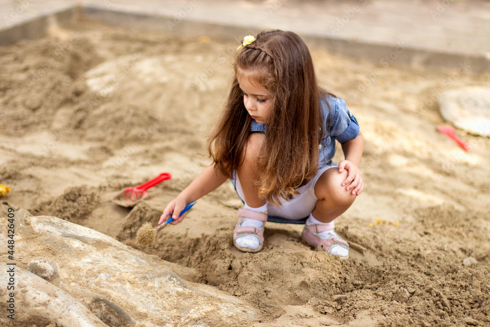 Foto de Cute little girl digging sand to find bones in the sandbox. do ...