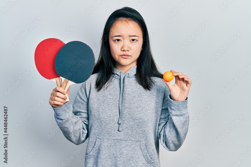 Young chinese girl holding red ping pong rackets and ball depressed and ...