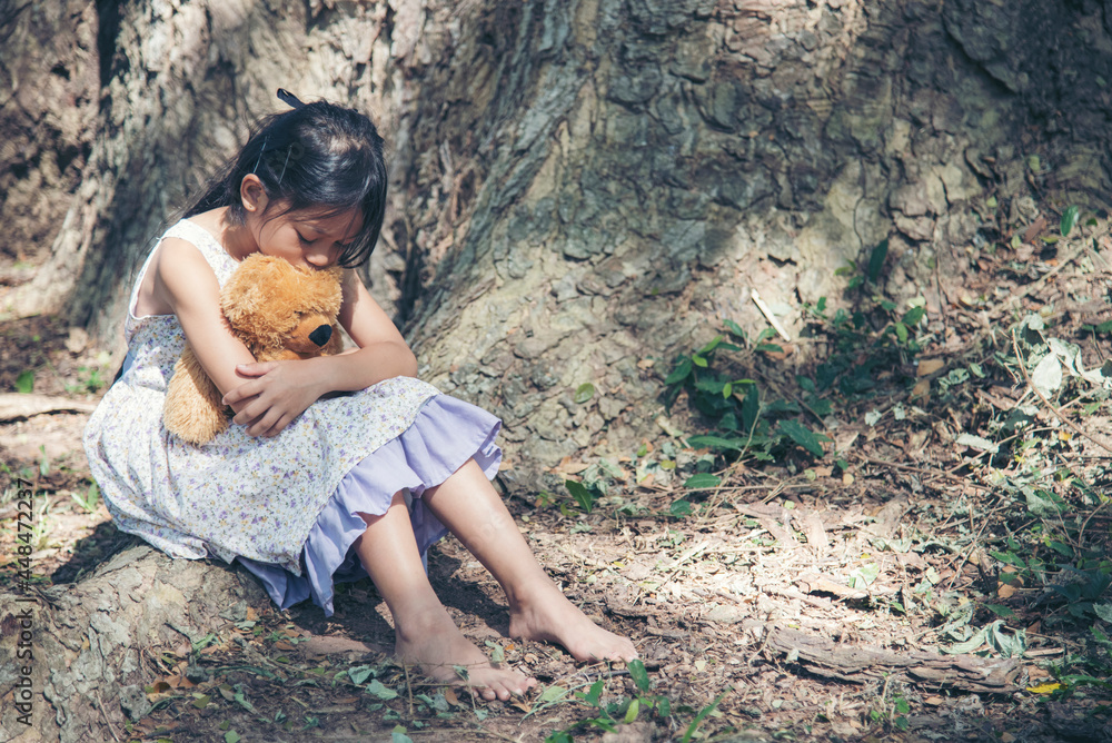 Sad girl hugging teddy bear sitting under tree sadness alone in green ...