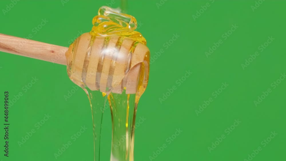 4K. Close up fresh honey pouring and flowing from wooden dipper spoon ...