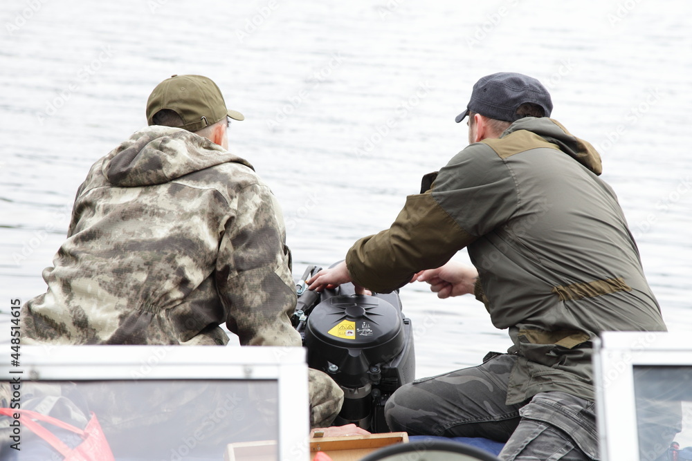 Two Caucasian men start an outboard boat motor with rope on the transom ...