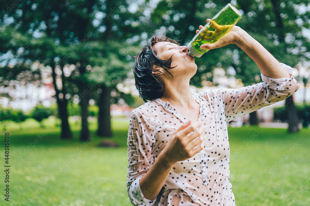 Wet woman fresh up and drink water from reusable bottle on hot summer ...