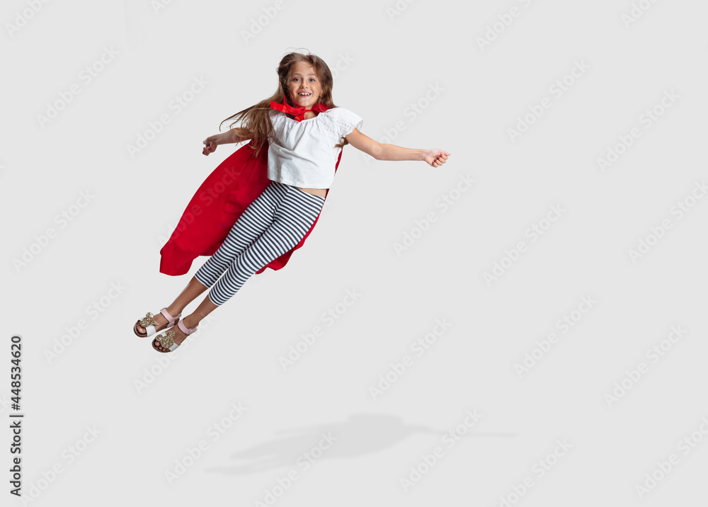Full-length portrait of beautiful little girl flying like super hero in ...