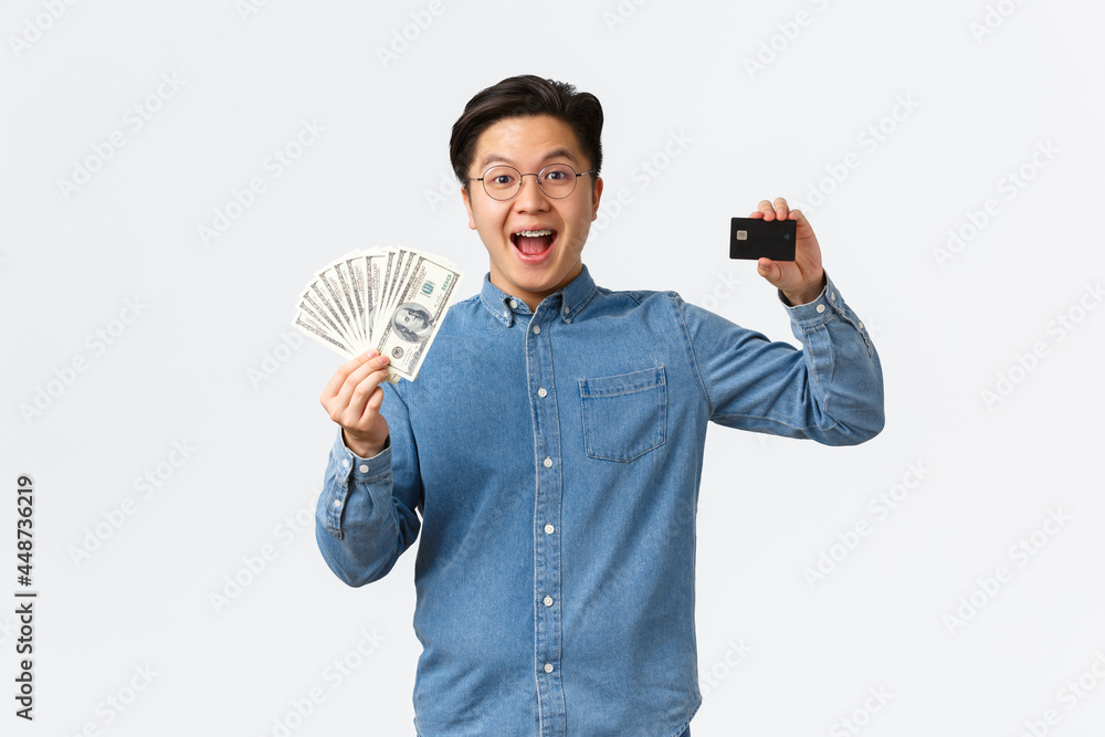 Enthusiastic asian businessman, young guy showing money and credit card ...