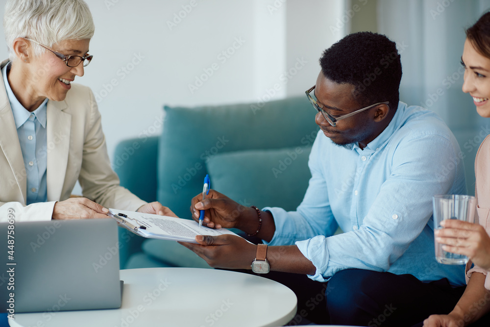 Happy black man signing an agreement while being with his wife on a ...