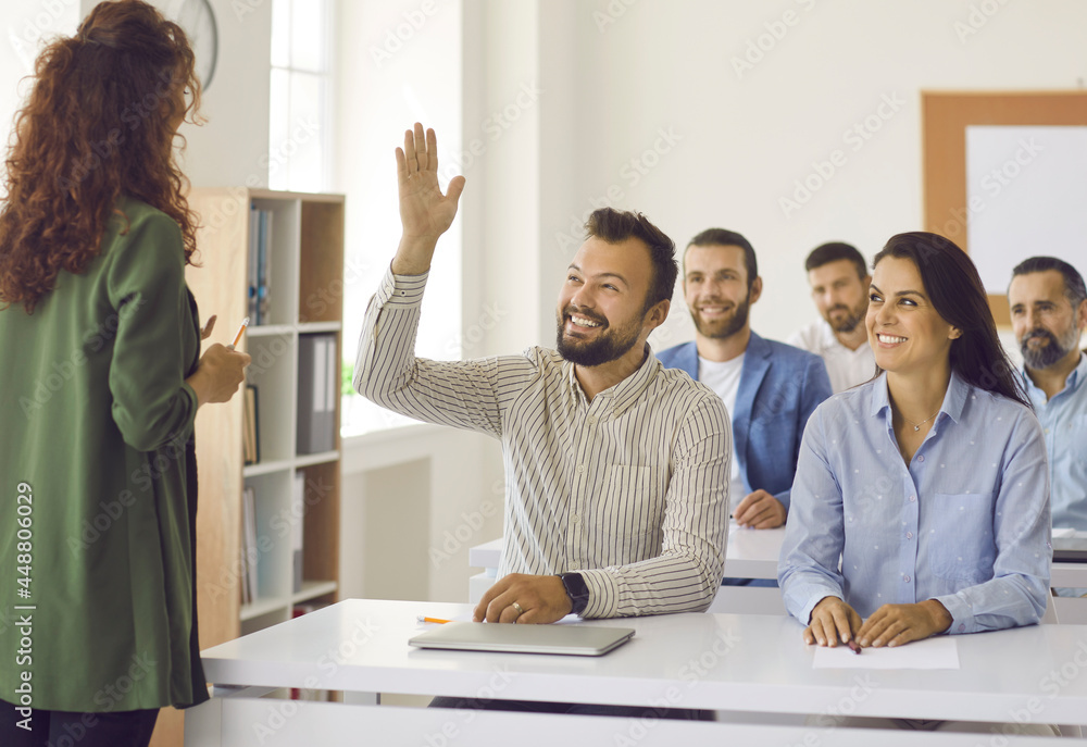 Smiling positive adult student raises hand to ask speaker a question ...