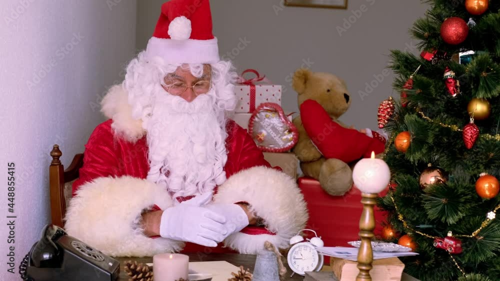 Santa claus in a traditional red costume with a white beard sits near a ...