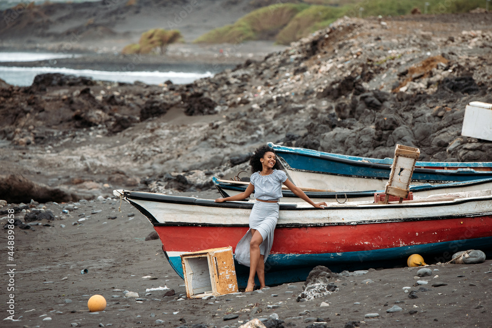Black woman leaning on boat near seashore with the ocean background ...