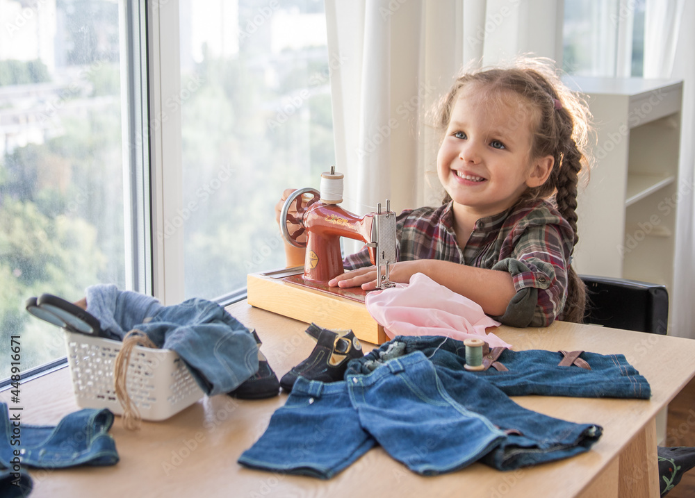 A little girl sews clothes for dolls on a toy sewing machine, a child ...