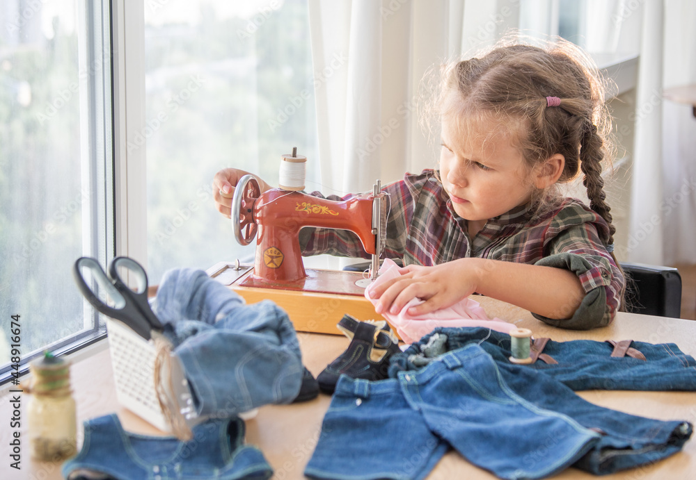 A little girl sews clothes for dolls on a toy sewing machine, a child ...