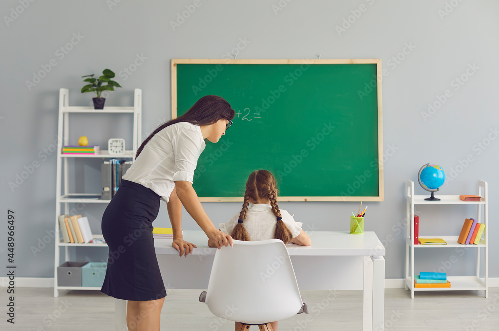 Female teacher helping little girl on math lesson at classroom, space ...