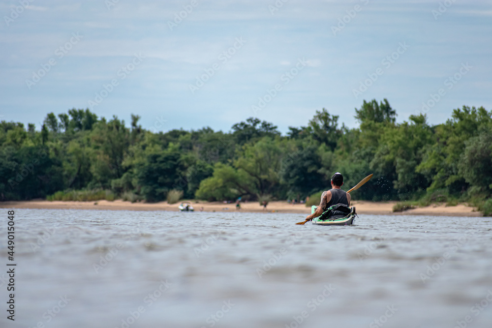 Hombre remando en kayak en el rio con arboles de fondo y una playa ...
