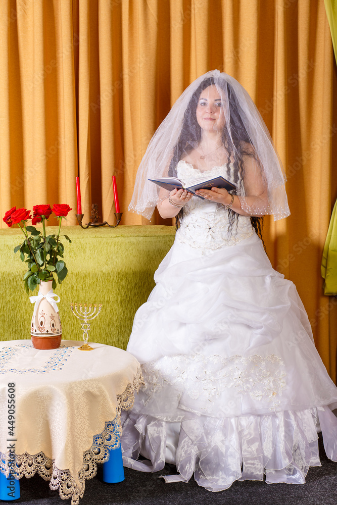 Jewish bride in a white dress, veiled face at a table with flowers ...