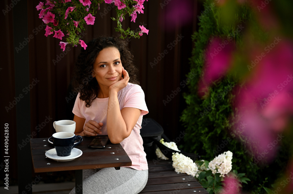 Beautiful woman sits at a table on the summer terrace of a cozy ...
